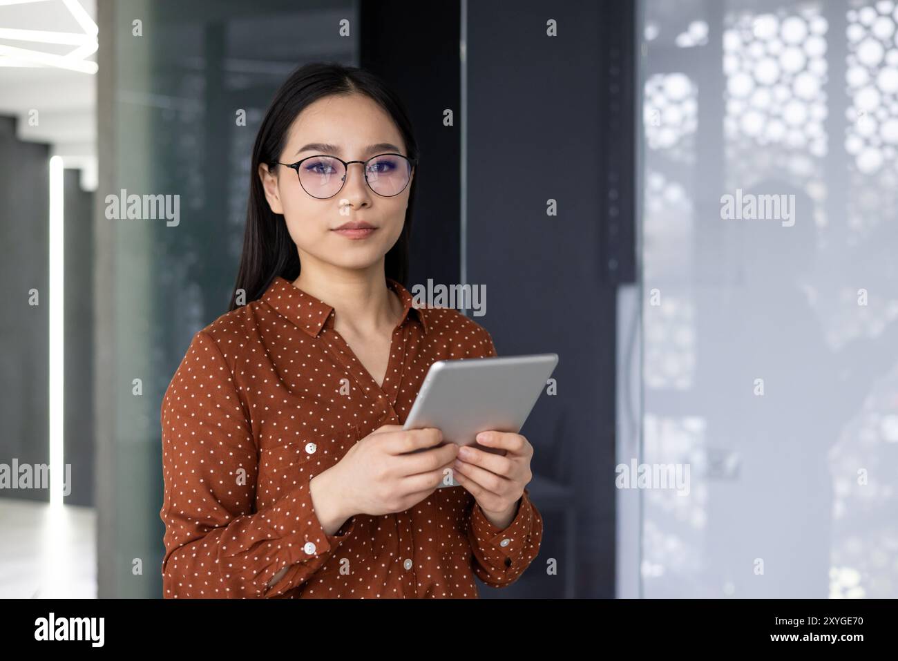 Asian worker confidently holding tablet device in modern office setting ...