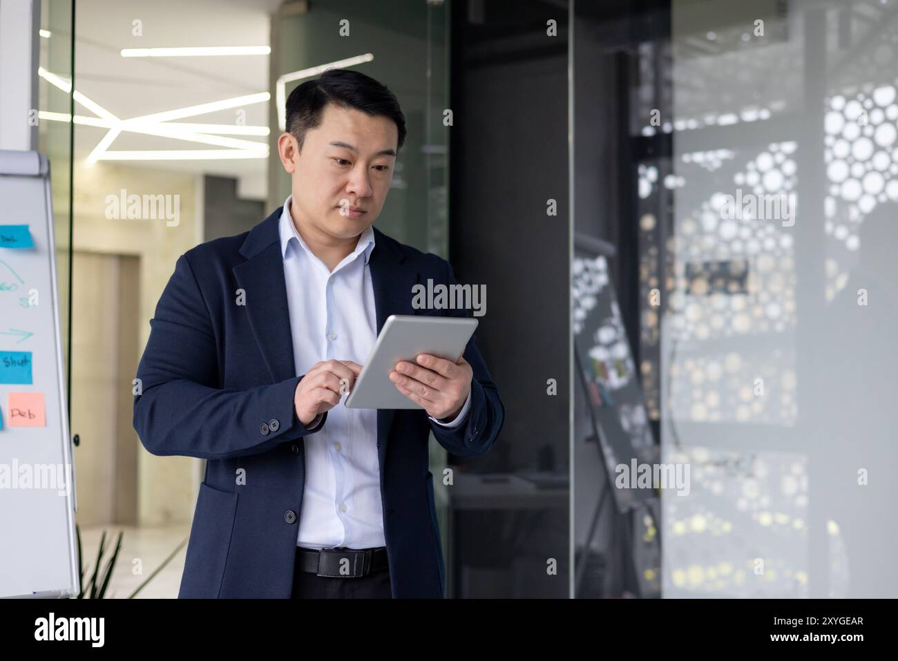 Asian worker intently using tablet in office, engaging with digital ...