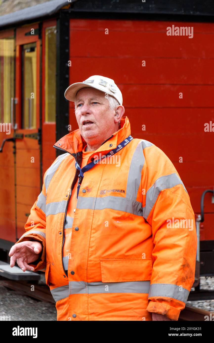 Railway worker in an orange safety jacket standing in front of a red ...