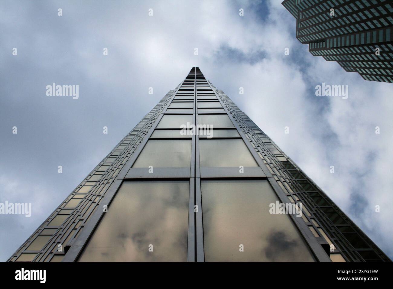 A towering skyscraper stretches towards a cloudy sky, its glass facade ...