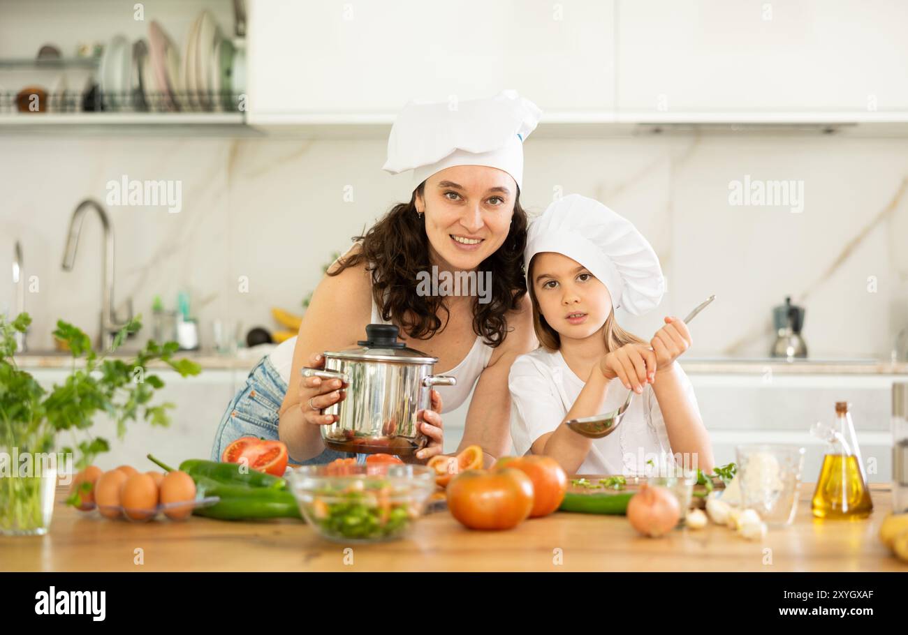 Mother and girl in white cooking hats are standing in kitchen near ...