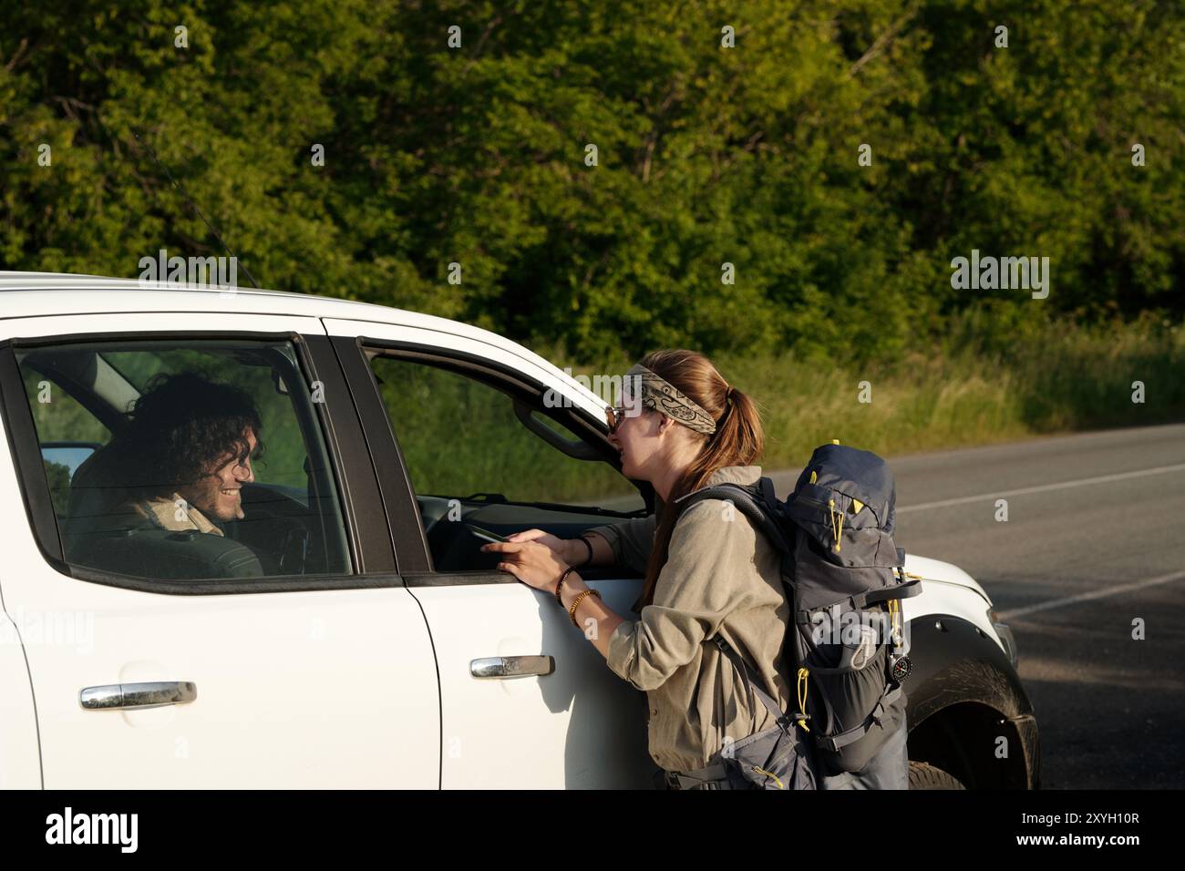 Young female hitchhiker with backpack standing by car window and ...