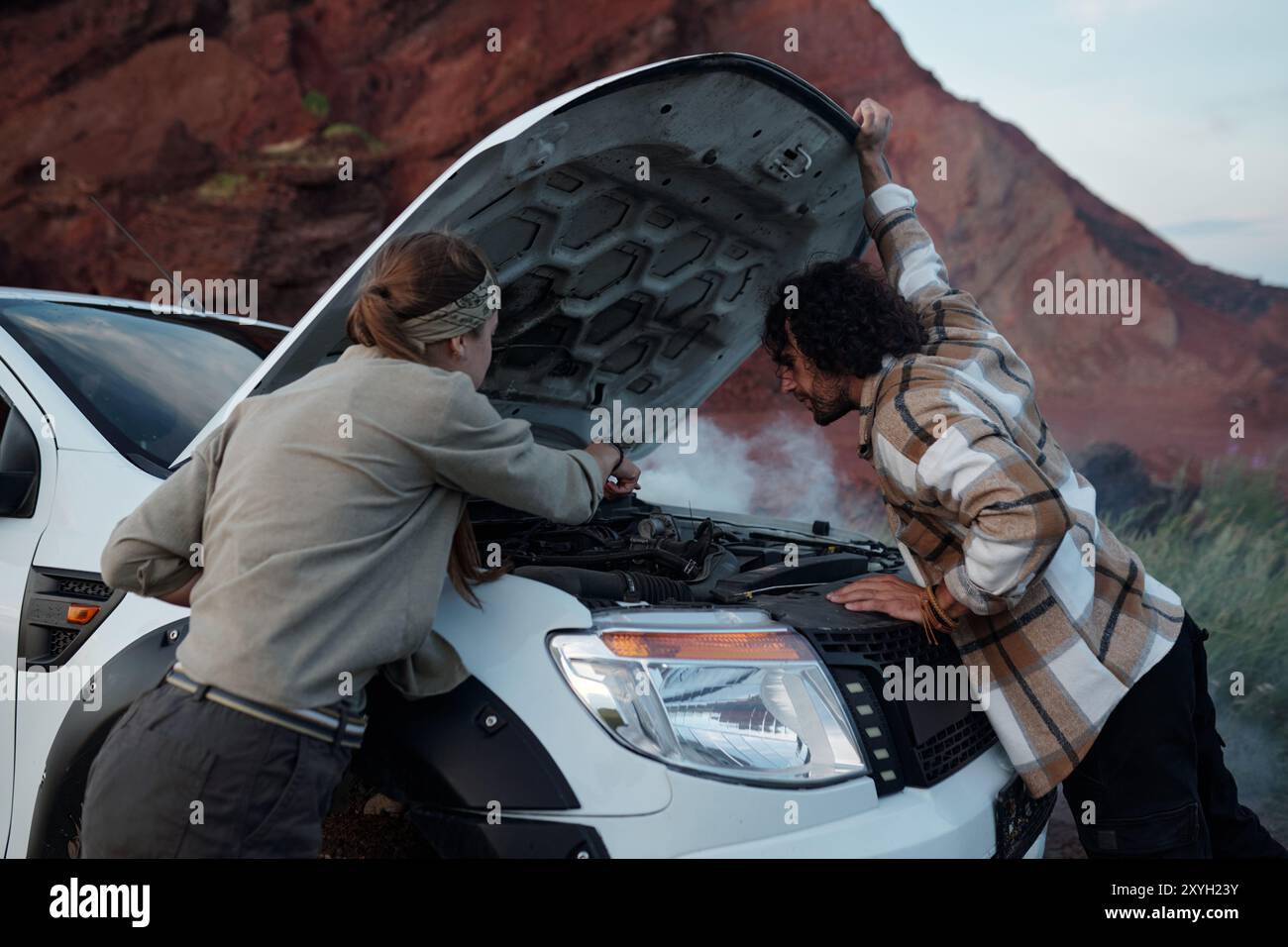 Young couple of travelers bending over engine of pickup truck while man ...