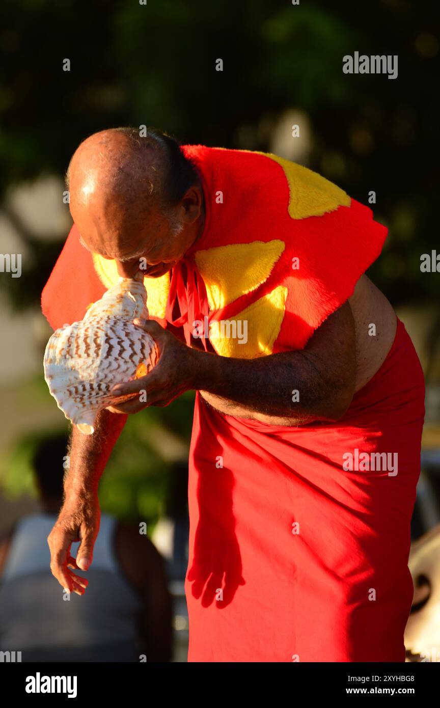 An elder blows into a large conch shell at sunset continuing a ...