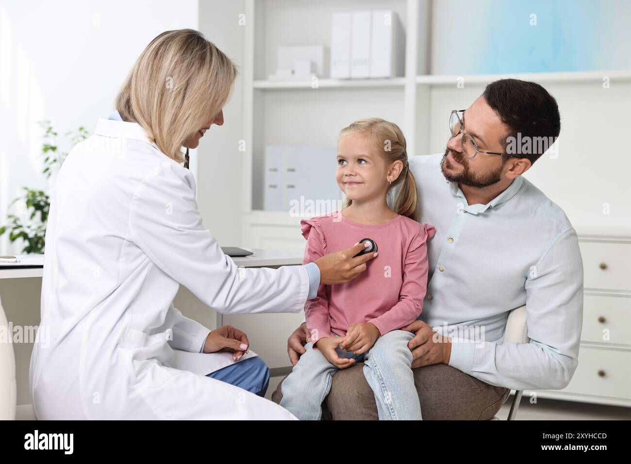 Doctor examining little girl with stethoscope and her father in ...