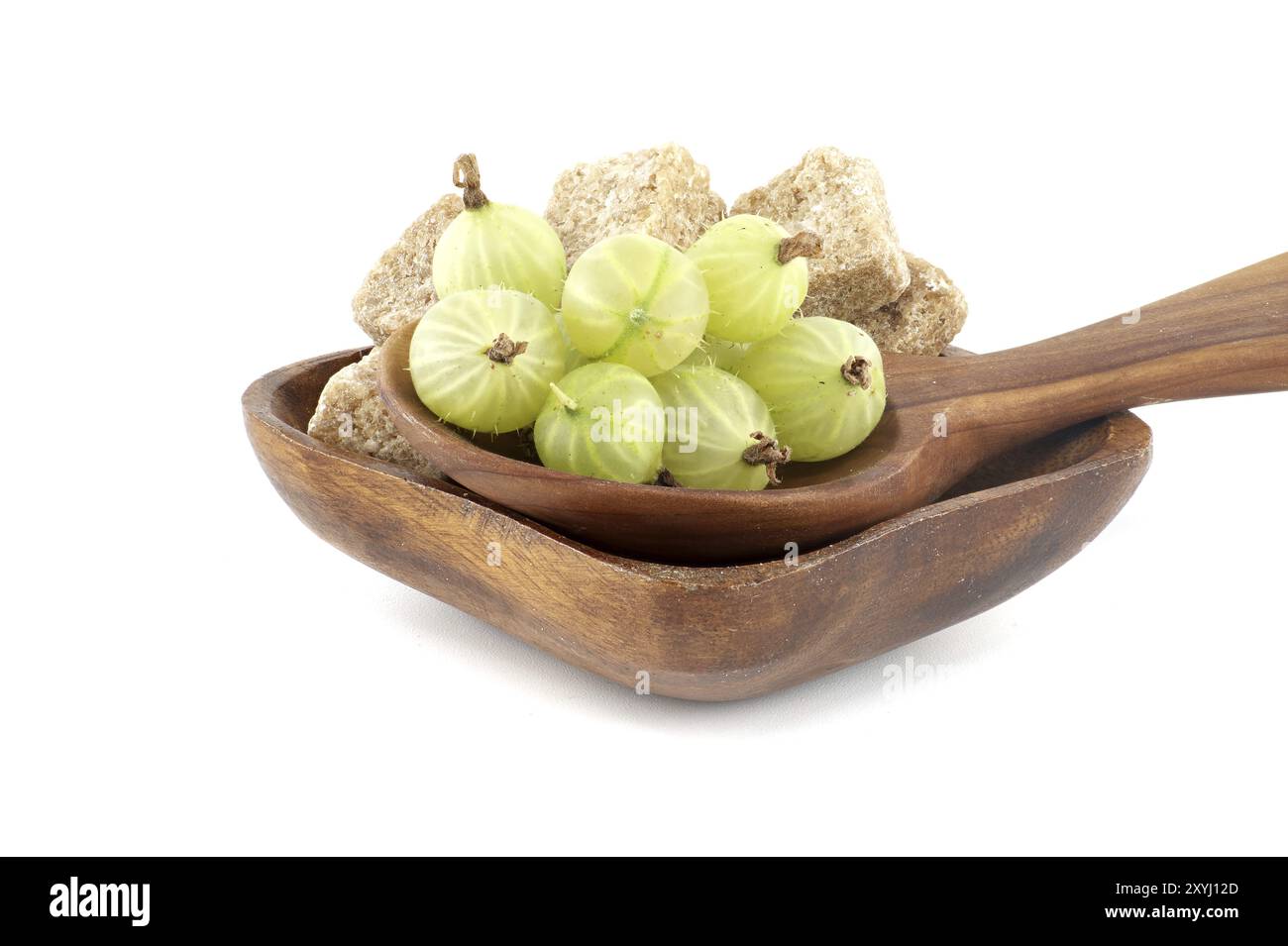 Green ripe gooseberries in a wooden spoon next to brown cane sugar ...