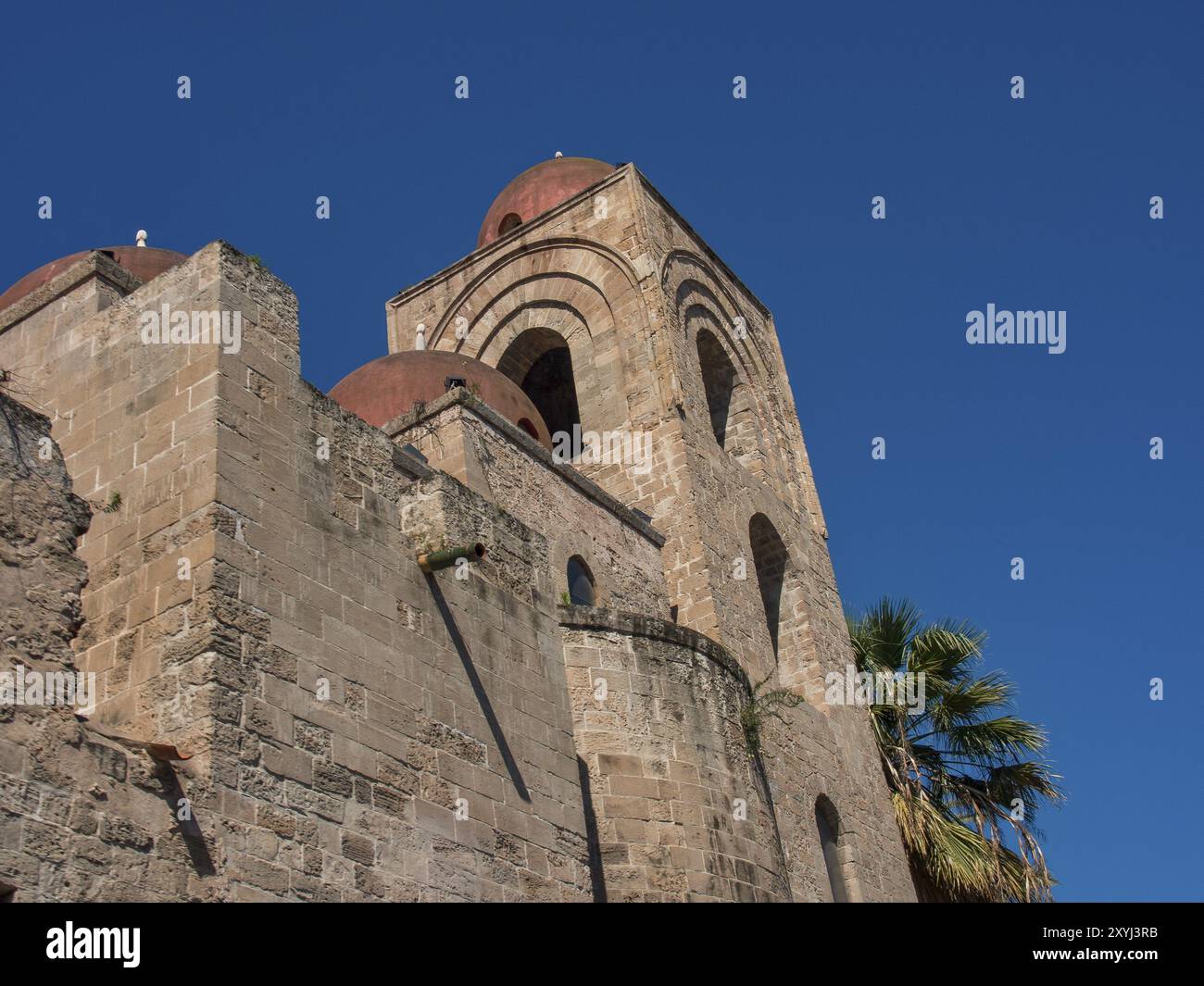 An old church tower with red domes and stone walls next to a palm tree ...