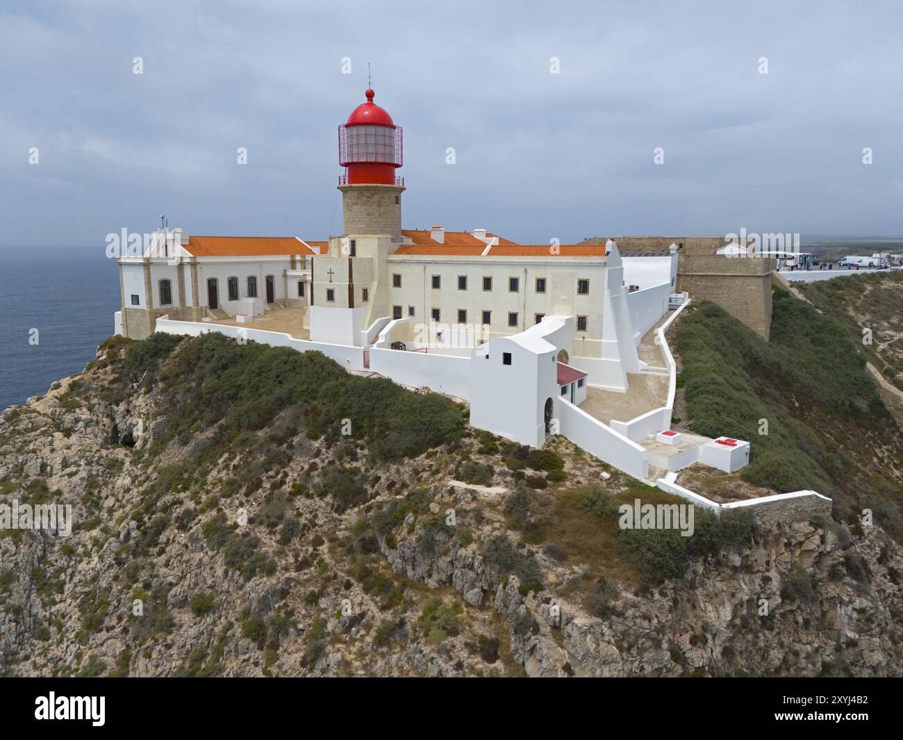 A red lighthouse and white buildings stand on a cliff, surrounded by ...