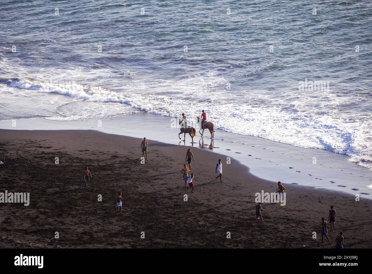 Two riders on horses ride along a beach, past people bathing Stock ...