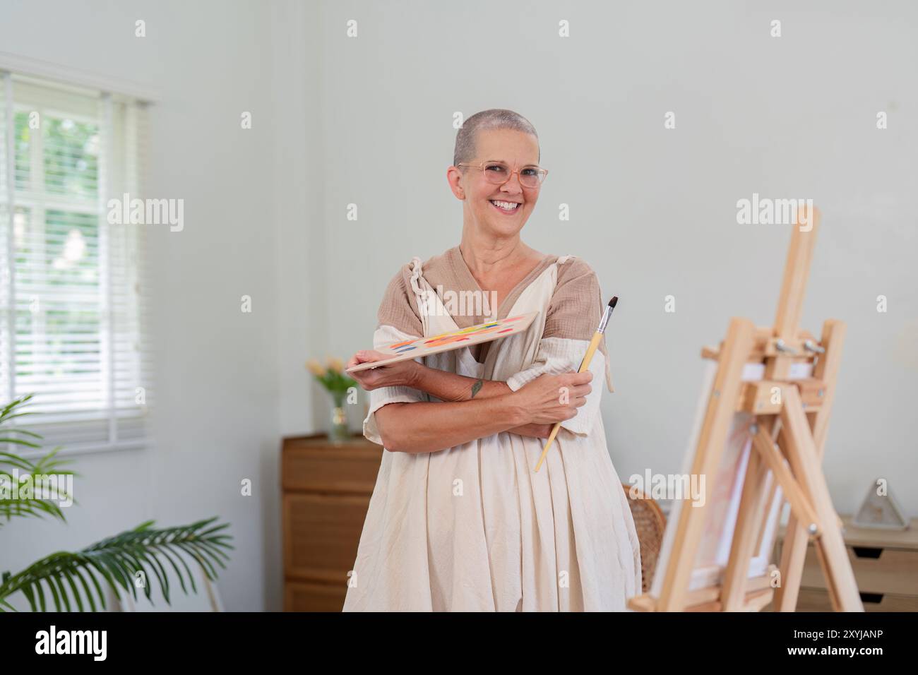 Smiling senior woman holding color palette by easel in studio Stock ...