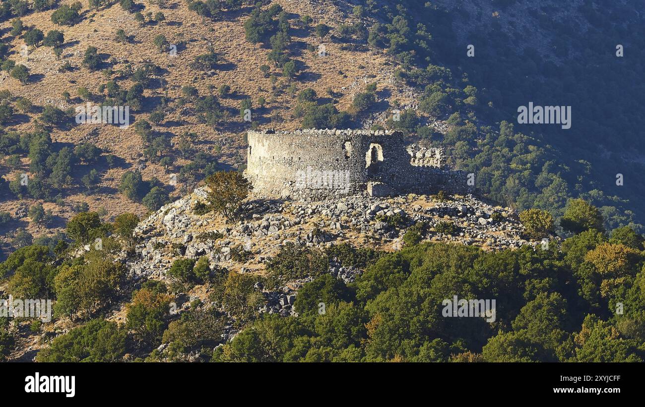 A medieval castle ruin on a hill surrounded by a wooded mountainous ...