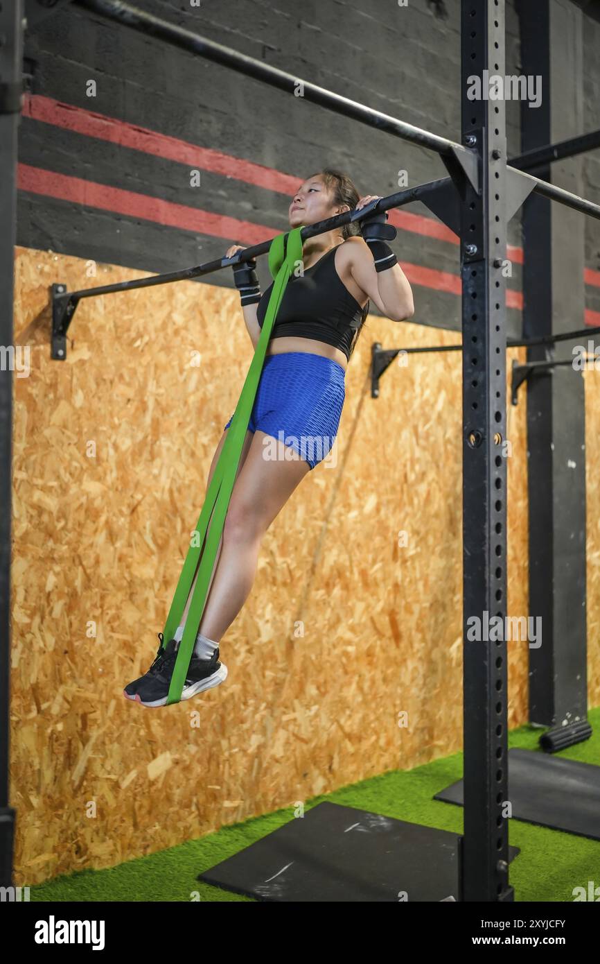 Vertical photo of a Chinese woman exercising doing pull-ups in the gym ...