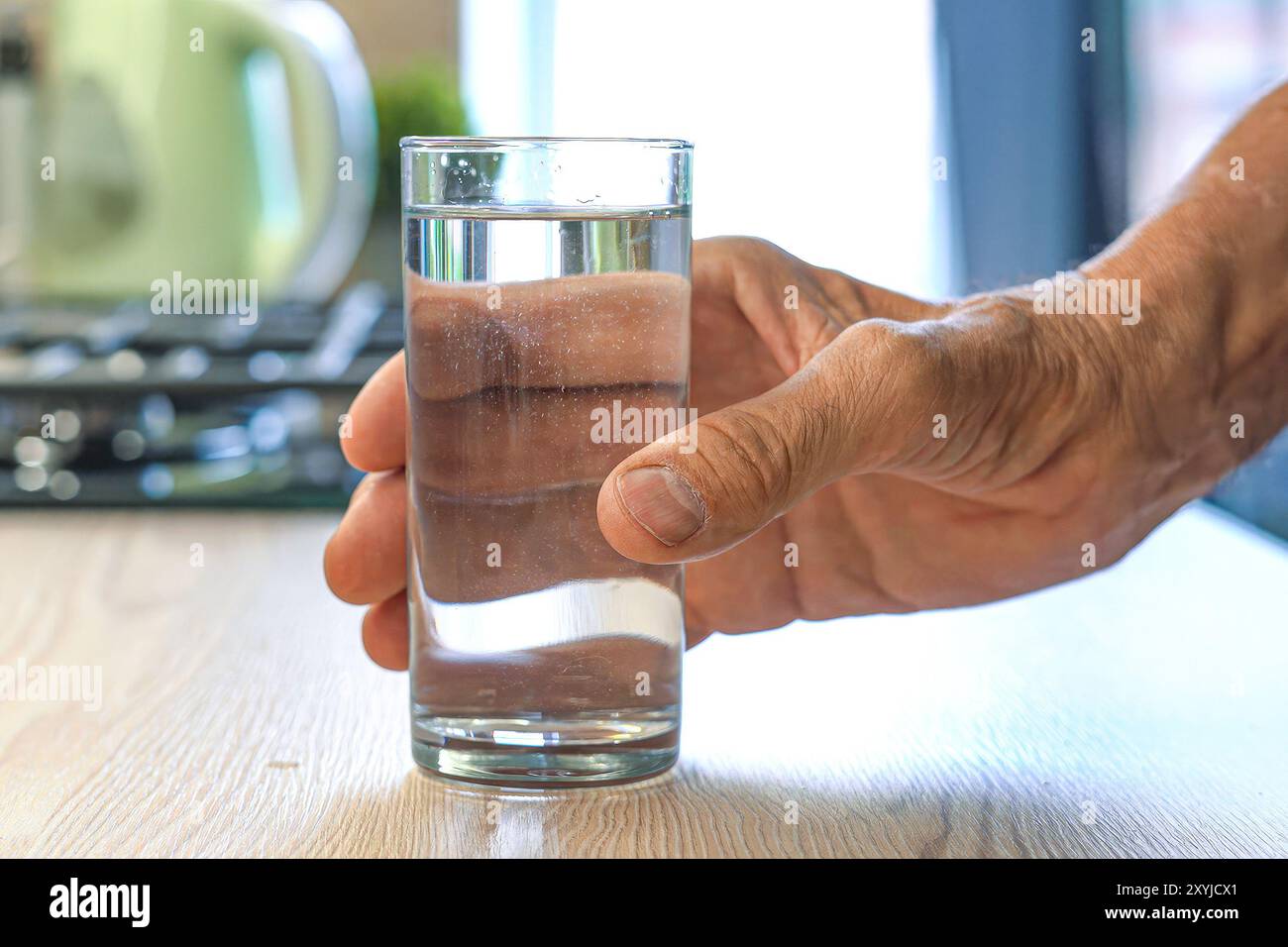 Hand holding glass of water on wooden table, representing calm moment ...