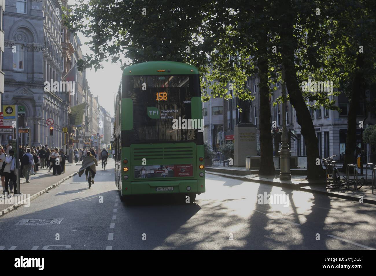 A green Irish bus makes its way through the leafy city centre on a ...