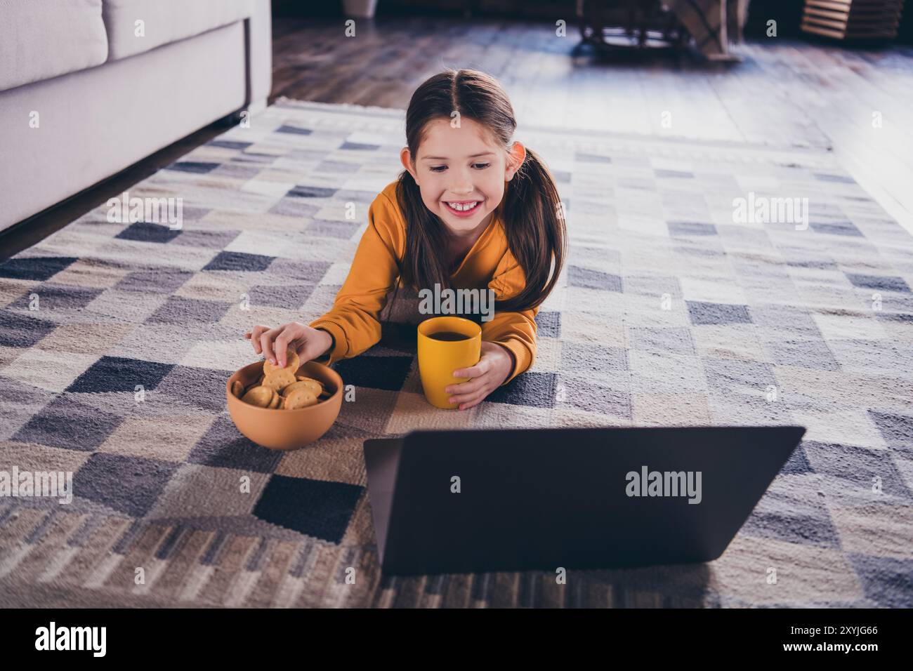 Full length photo of little girl lying floor watch movie snacks drink ...