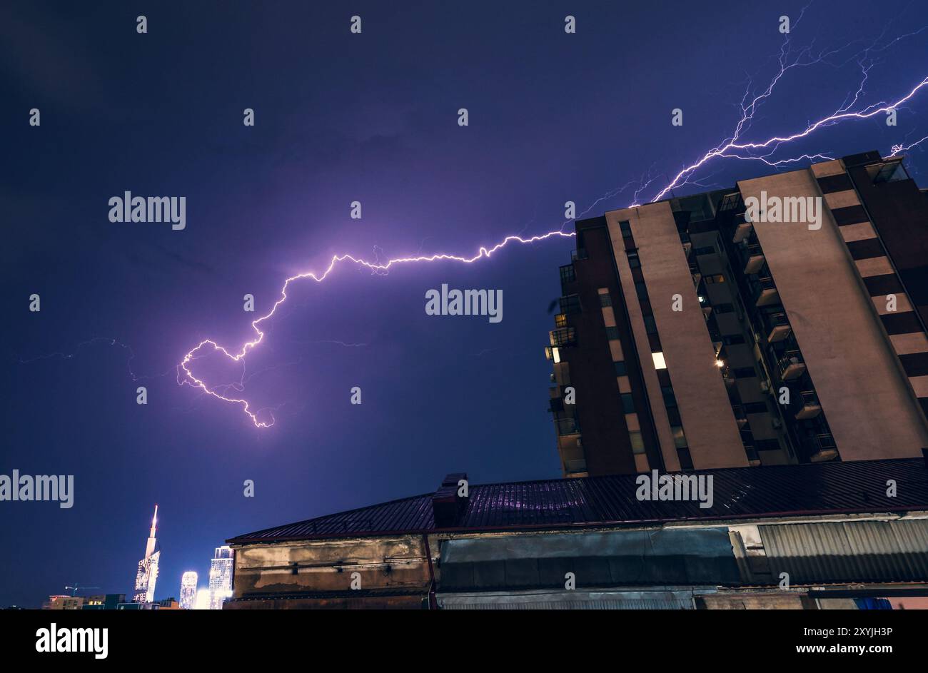 Lightning striking near urban buildings during thunderstorm at night ...