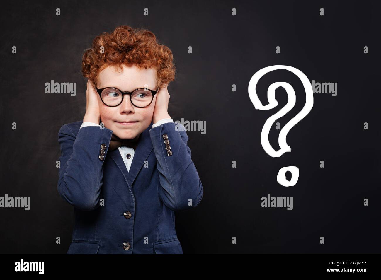 Unsure child boy school student covers his ears with his hands against blackboard background ...