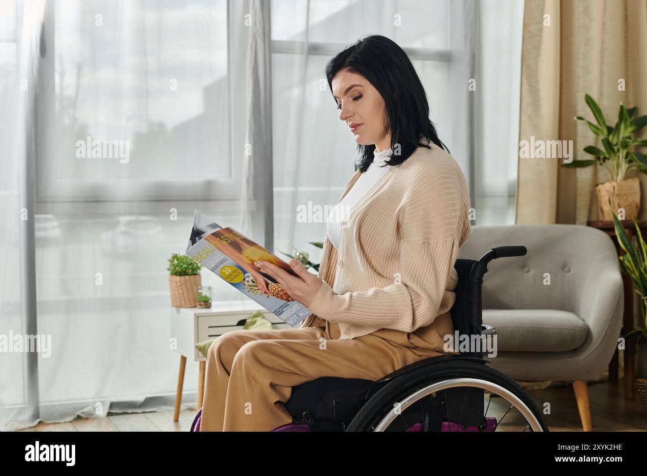 A woman in a wheelchair sits by a window, reading a magazine Stock ...