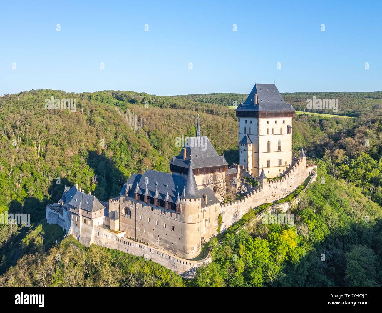 Karlstejn Castle, surrounded by lush green forests, on a sunny day. The ...