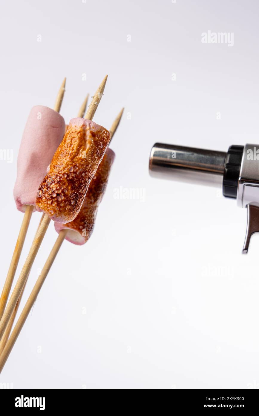 A vertical image showcasing marshmallow skewers being roasted by a ...