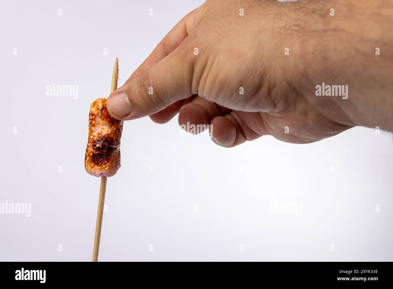 A detailed shot of toasted marshmallow skewers, with a hand grabbing ...
