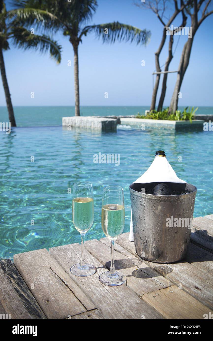 Champagne bottle in ice bucket and champagne glasses by swimming pool ...
