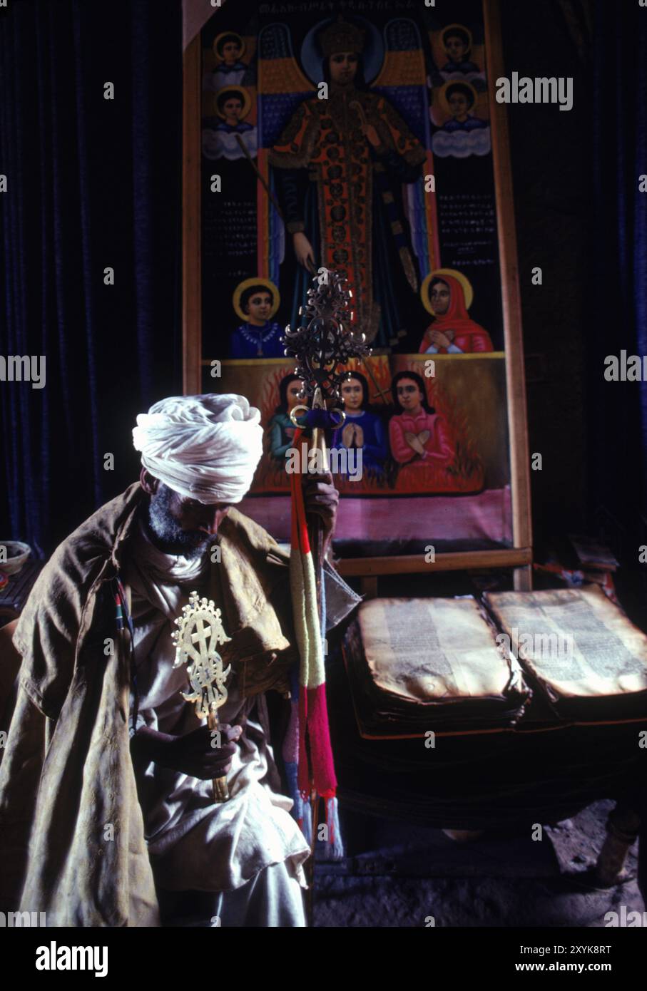 Monk with crucifix sits by hand written bible in church at Lalibela ...