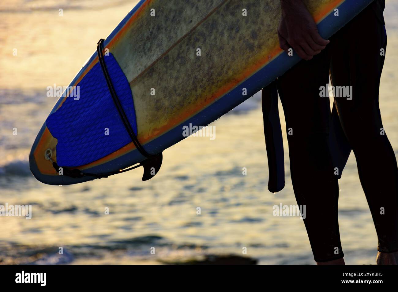 Detail of man seen from behind holding his surfboard in front of the ...