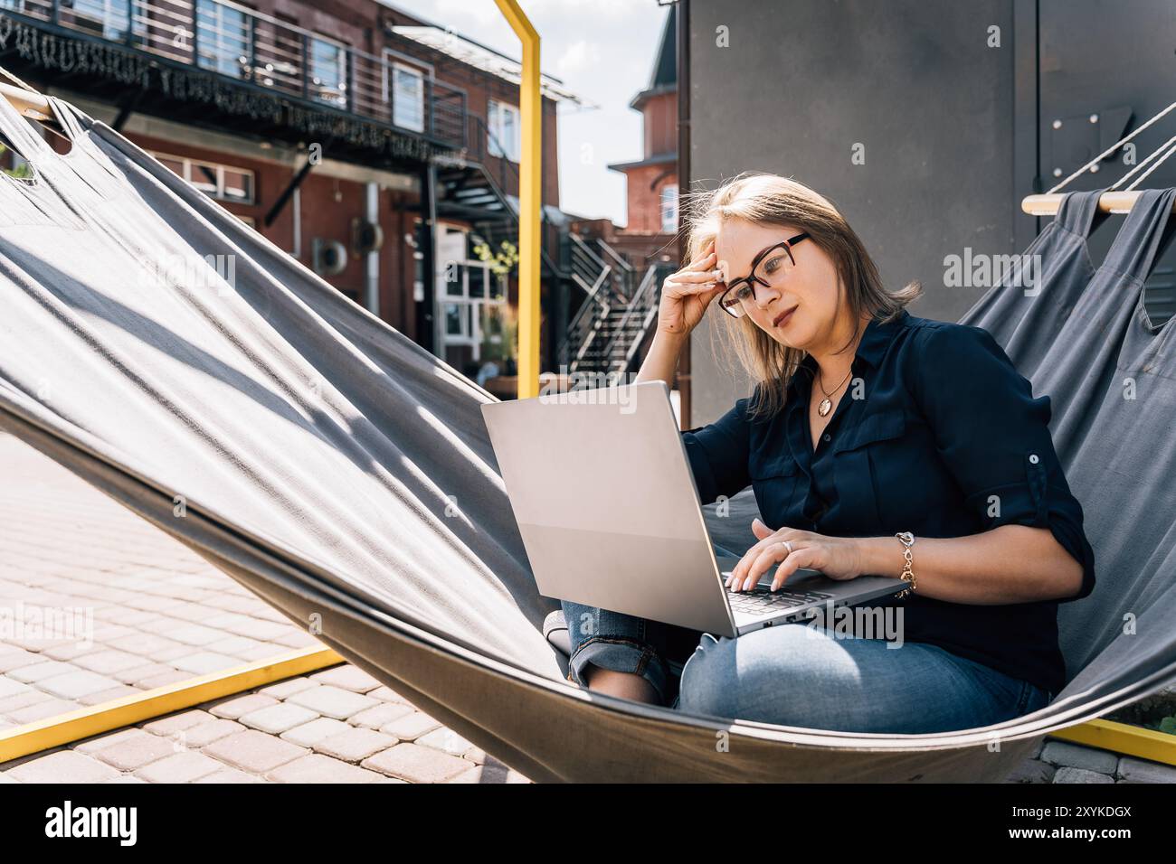 thoughtful woman solving complex problem on laptop in urban hammock ...