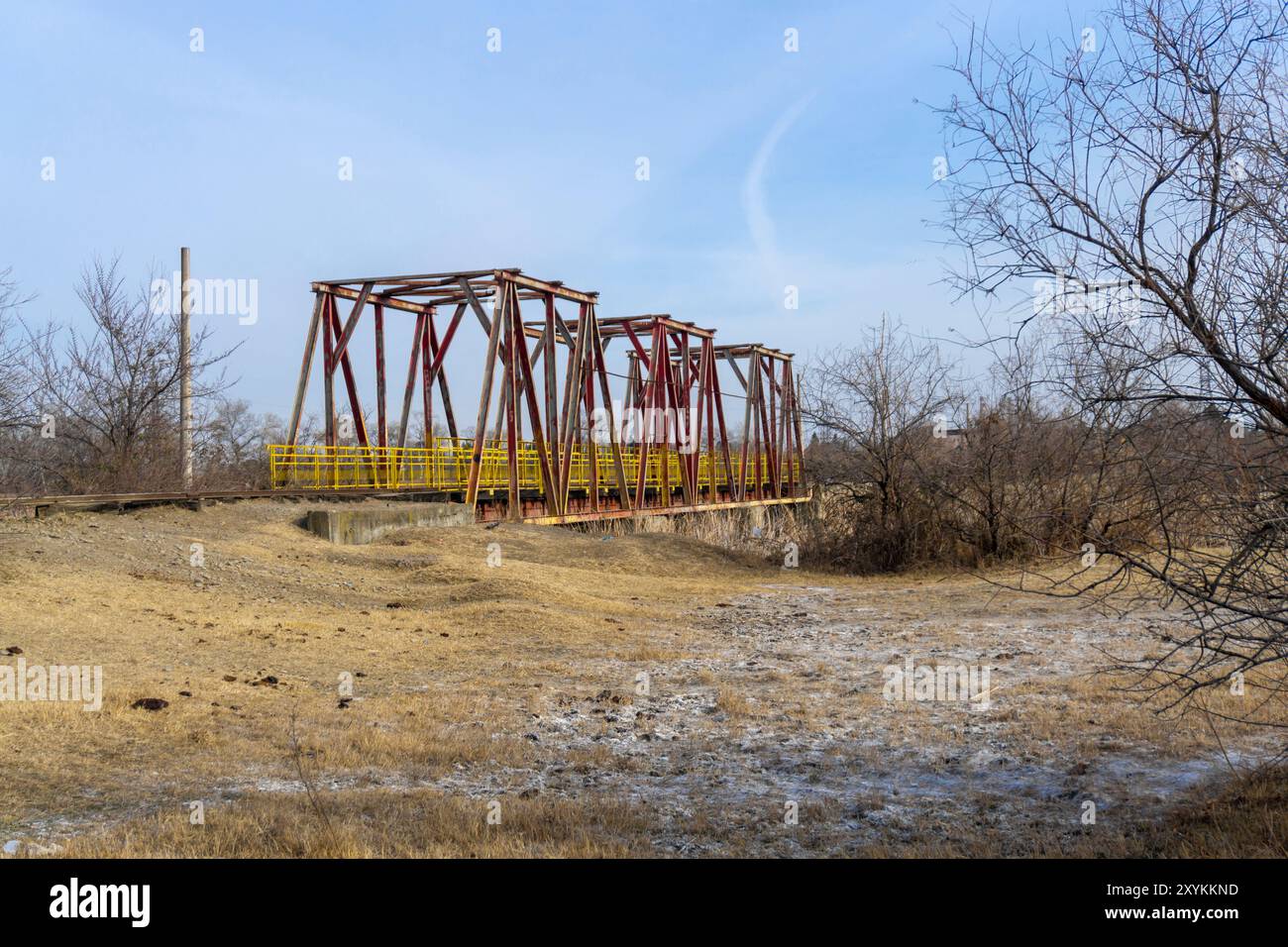 Multi-colored metal railway bridge over a ravine. Yellow grass, trees ...