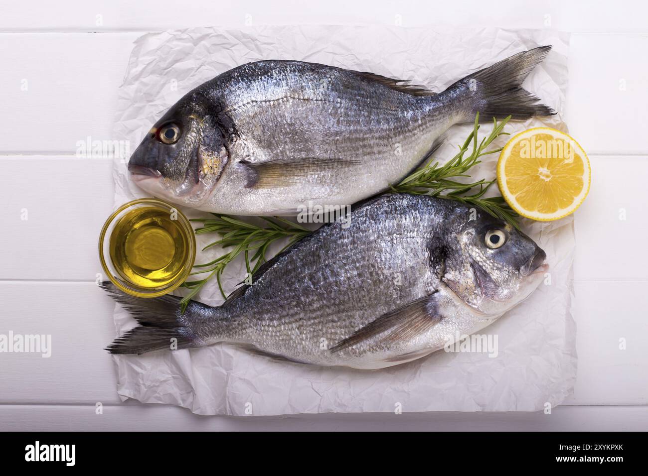 Fresh raw sea bream fish with lemon slices, salt, rosemary and olive ...