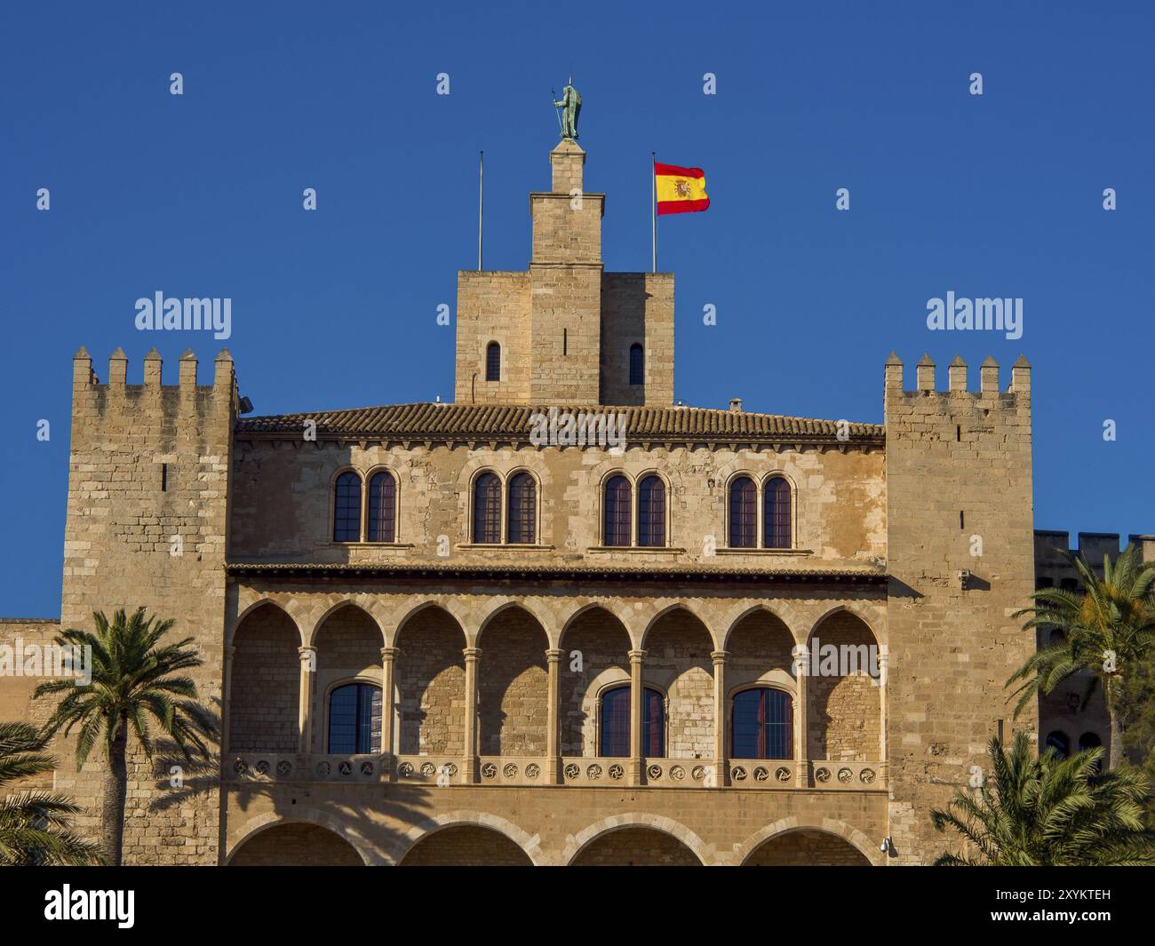 Facade of a castle with towers and Spanish flag in front of a blue sky ...