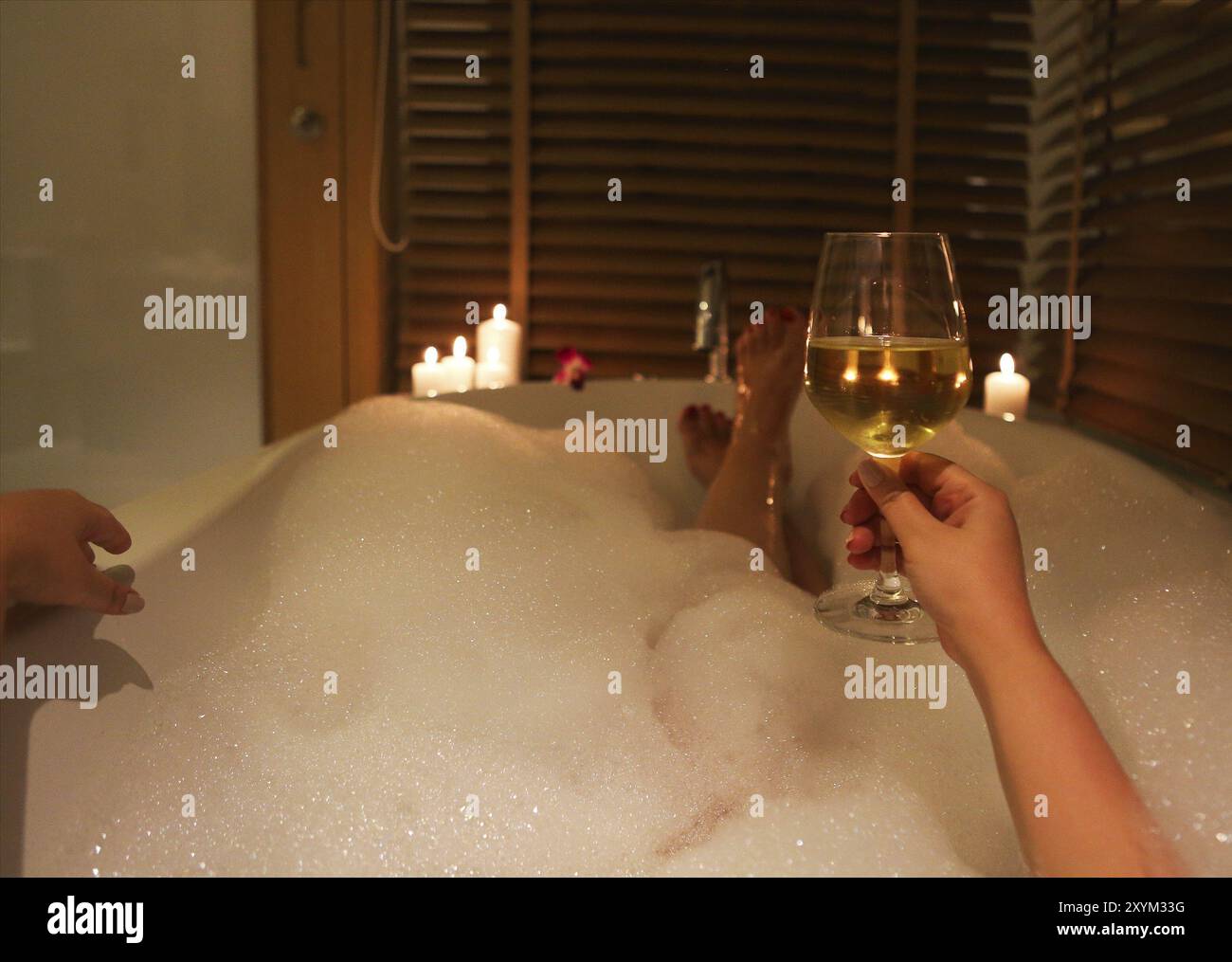 Back view of the feet of the young woman drinking white wine in bath ...