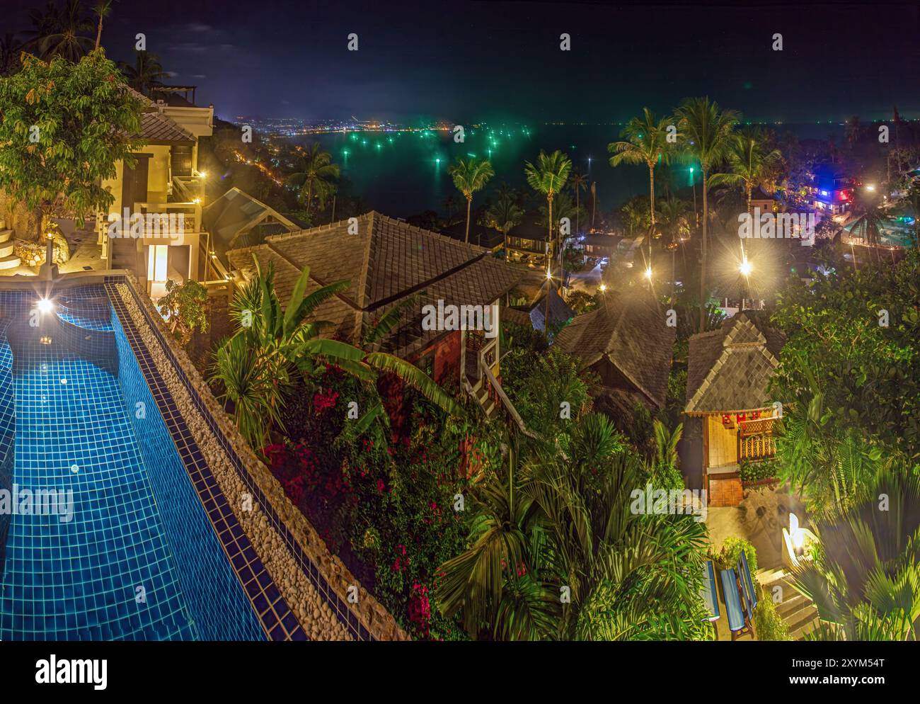 View over an infinity pool on a slope above a tropical beach at night ...
