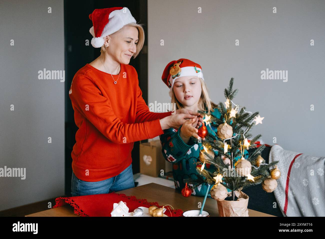 Mother and daughter decorating Christmas tree together, holiday bonding ...