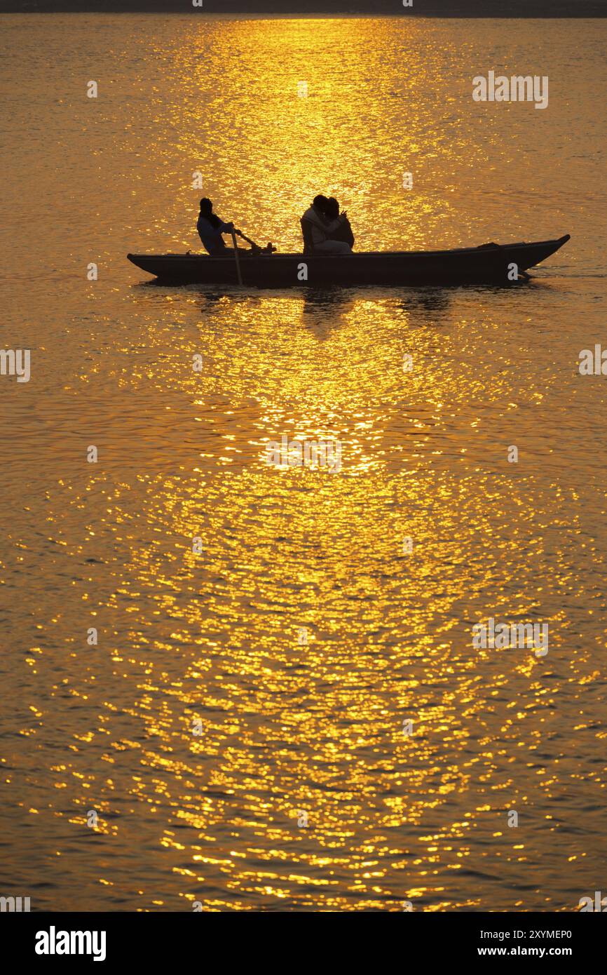 Silhouettes of Indian tourists take a sunset rowboat ride on the Ganges ...