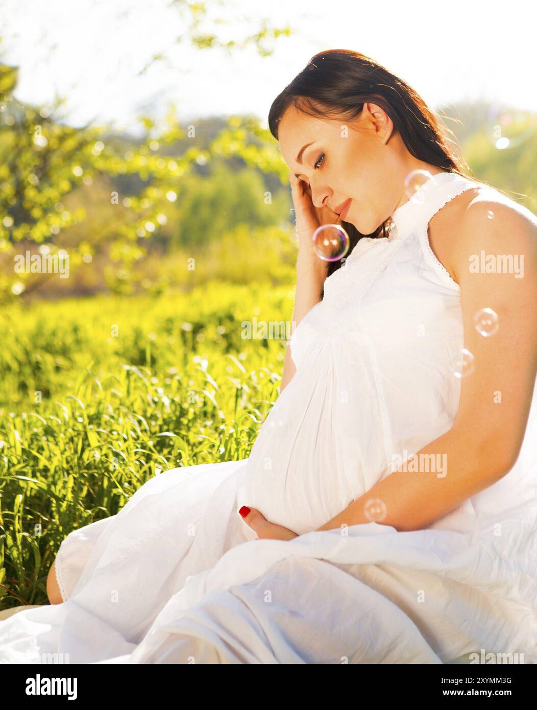 Portrait of beautiful pregnant woman in white dress in the flowering ...