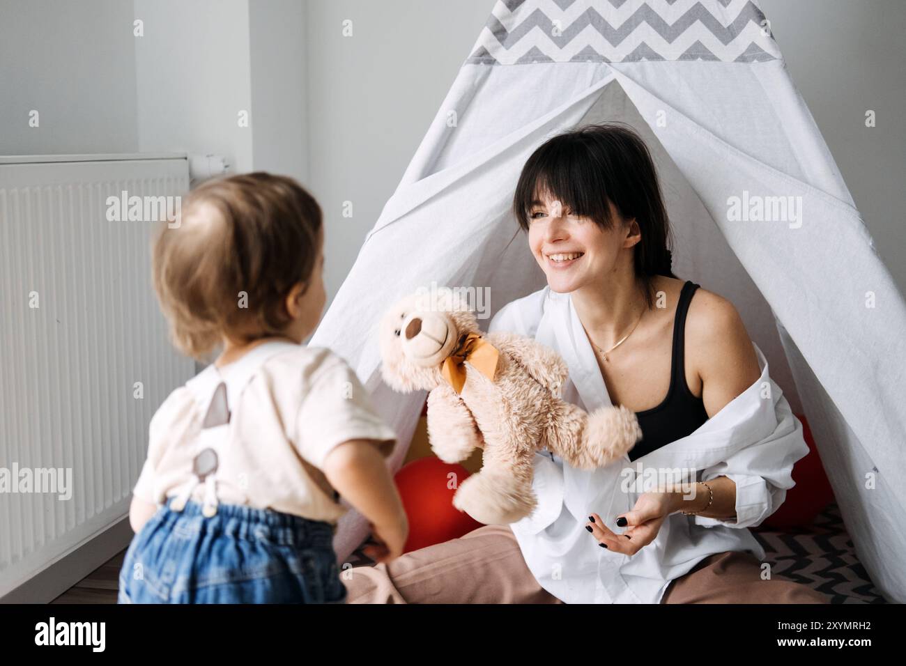 Mother playing with toddler using a toy bear in an indoor tent. Parent ...