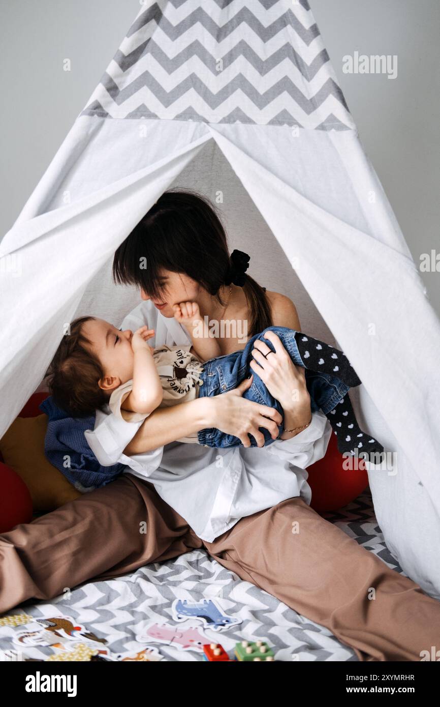 Mother and toddler playing together in a cozy indoor tent. Bonding, playtime, early childhood ...