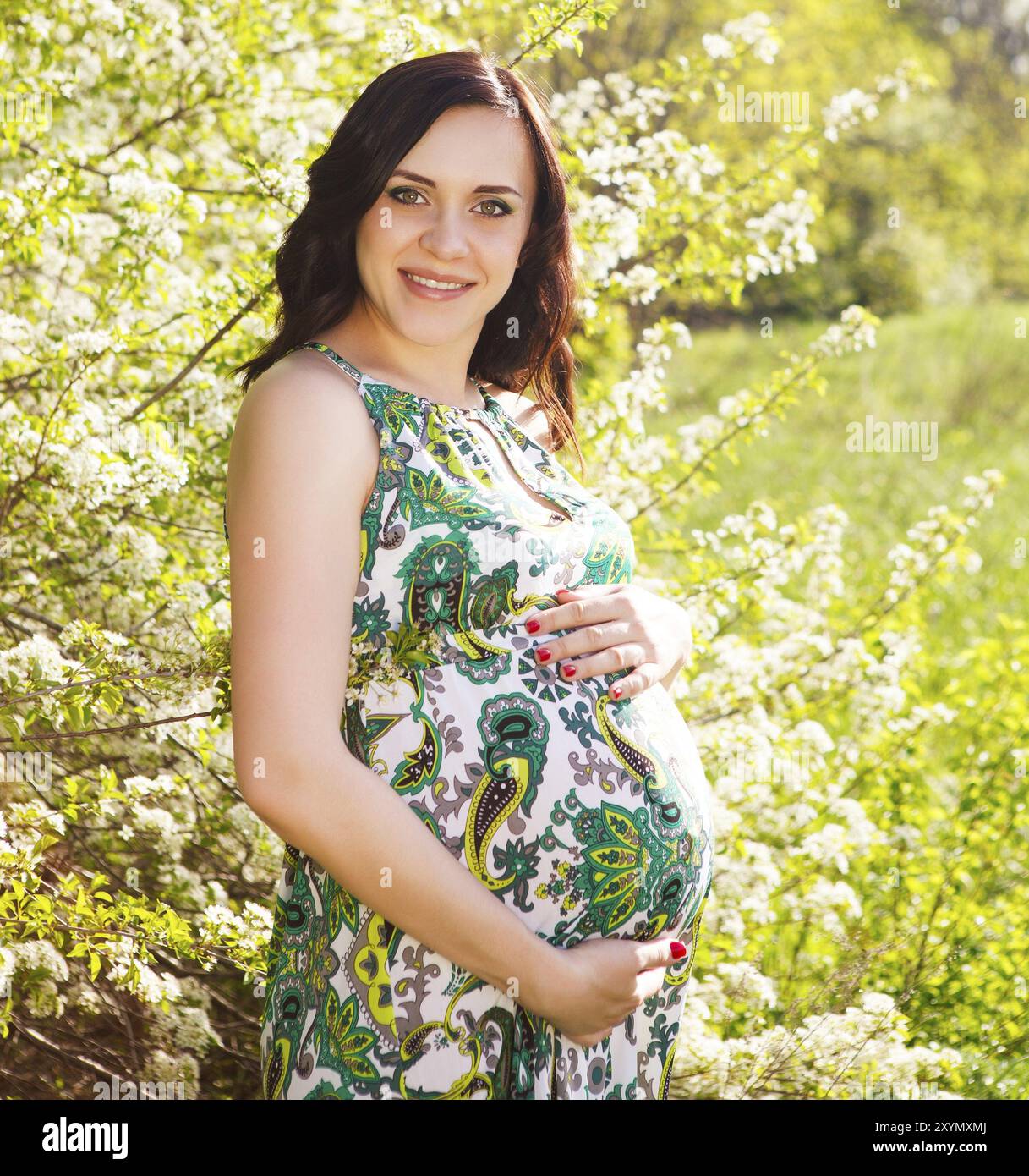 Portrait of beautiful pregnant woman in green dress in the flowering ...