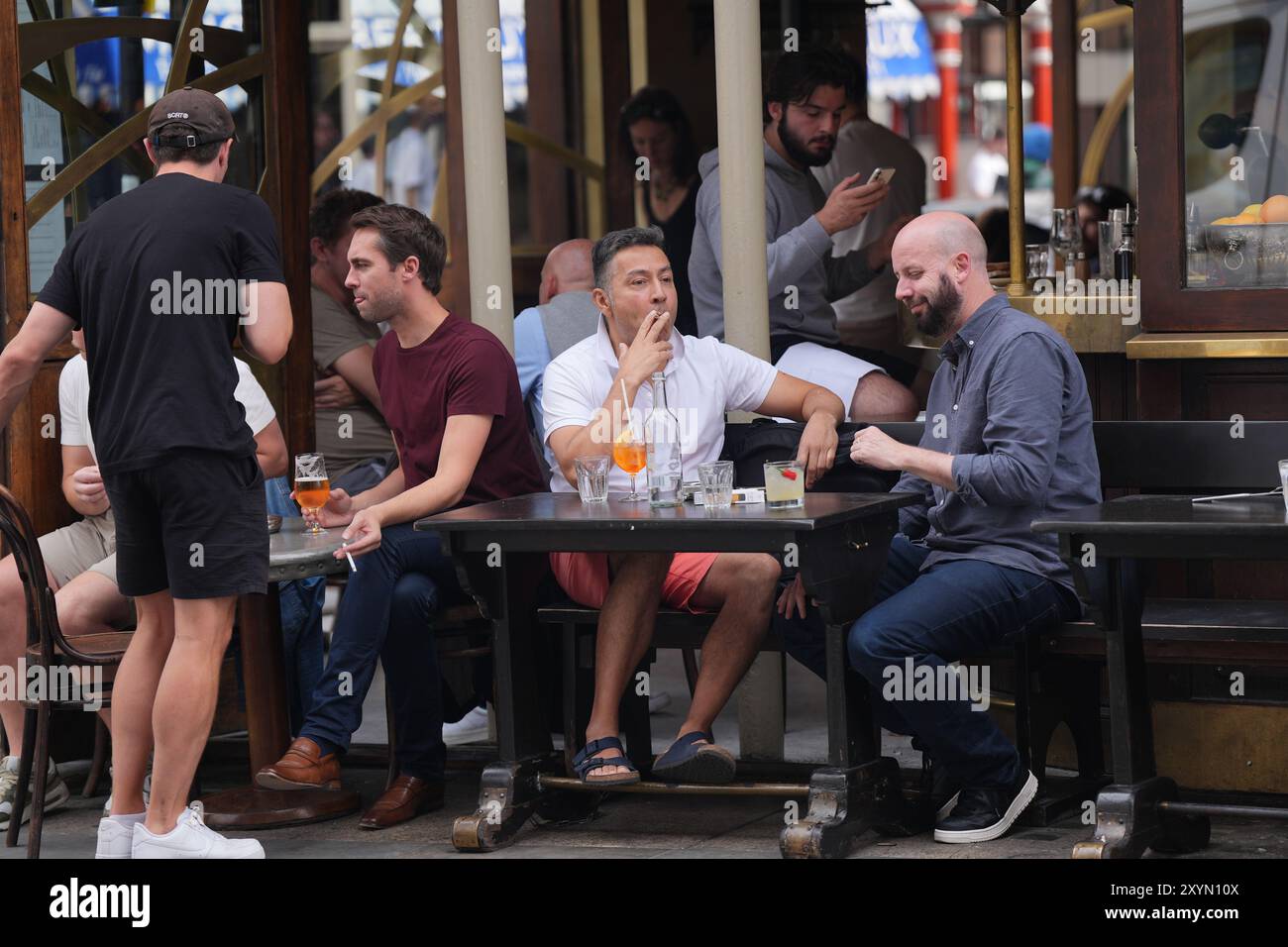 A person smoking a cigarette while sitting outdoors in a pub, in Soho ...