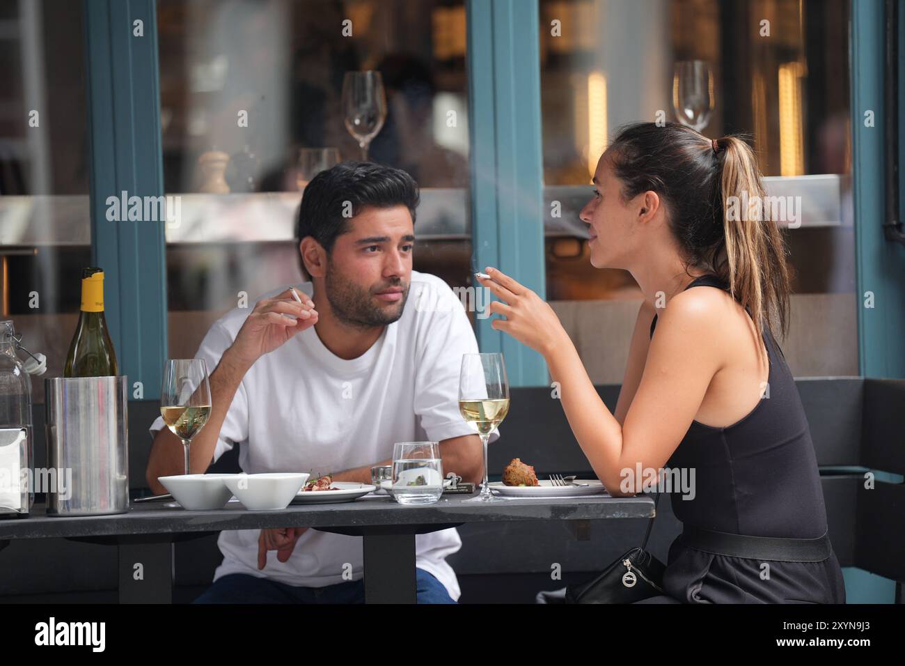 People smoking cigarettes while sitting outdoors at a restaurant, in ...