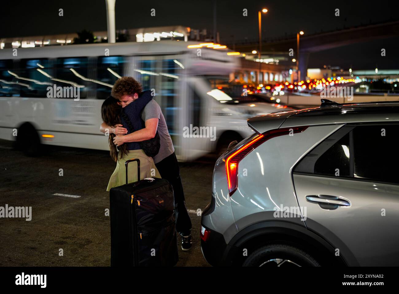 Two people hug goodbye as traffic congestion builds around parking ...