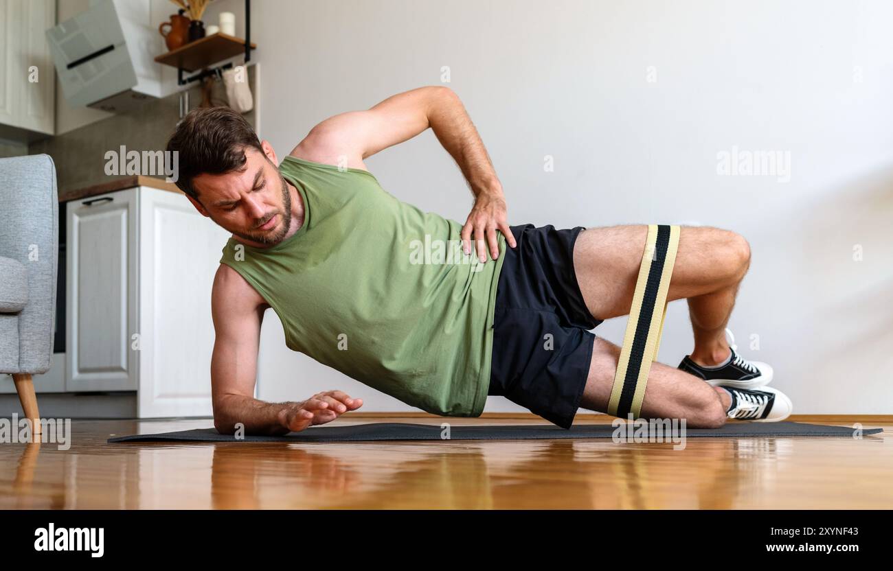Man in plank pose on yoga mat using a resistance band for leg strength ...