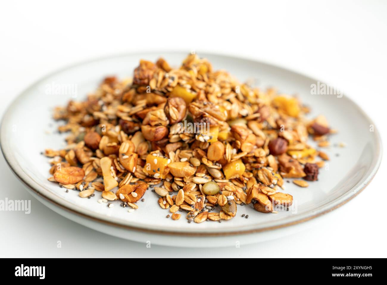 A bowl of granola with nuts and seeds on a white plate. The granola is ...