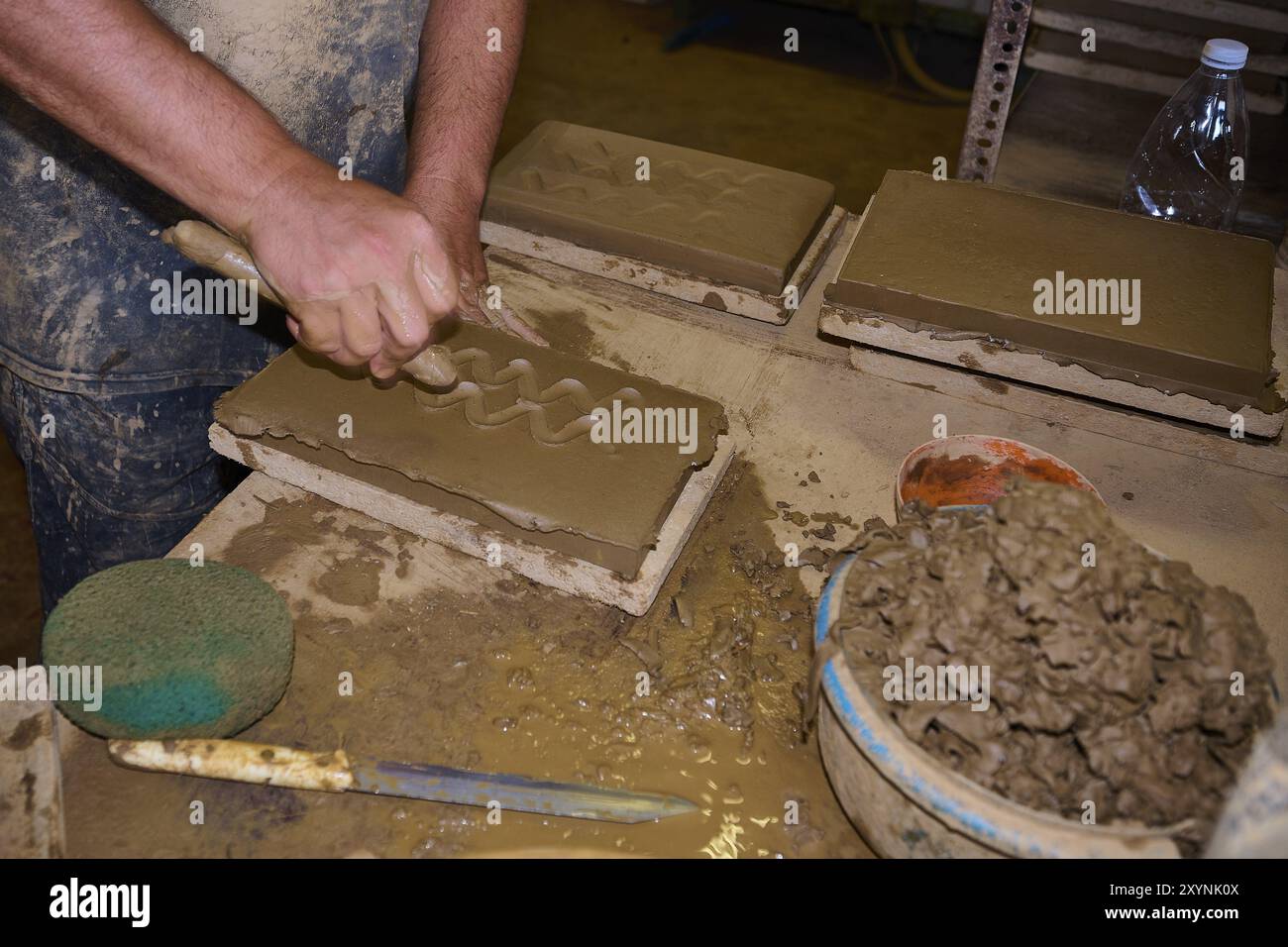 Worker's hand carving patterns in clay bricks, surrounded by clay and ...