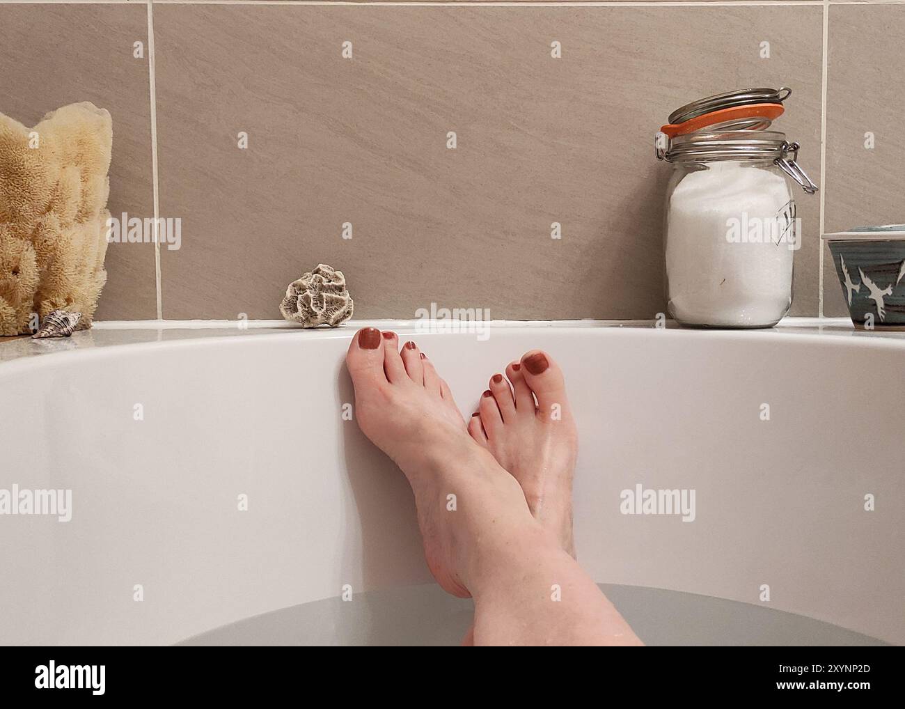 a pair of crossed feet with red painted toenails resting on filled bath ...