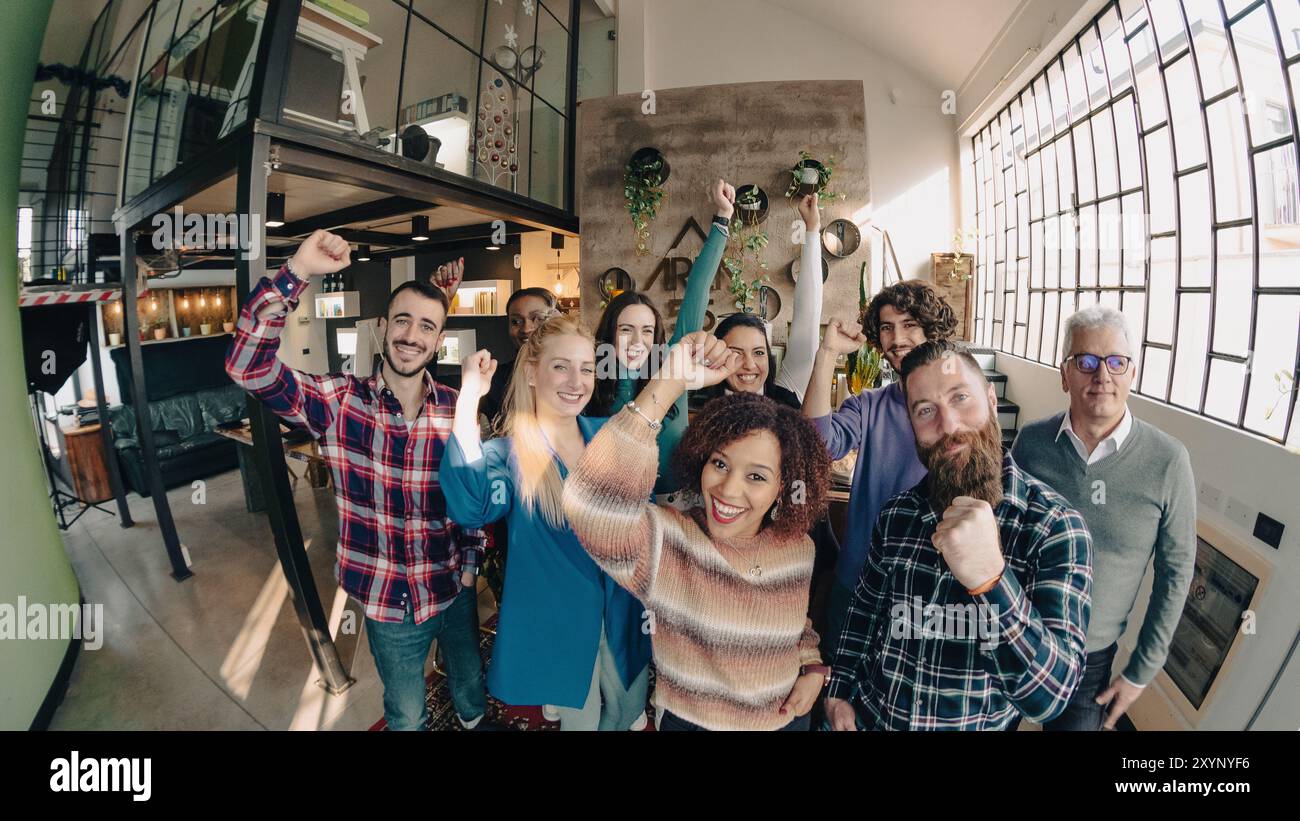 Group of cheerful coworkers raising their arms in victory to celebrate a success in their modern ...