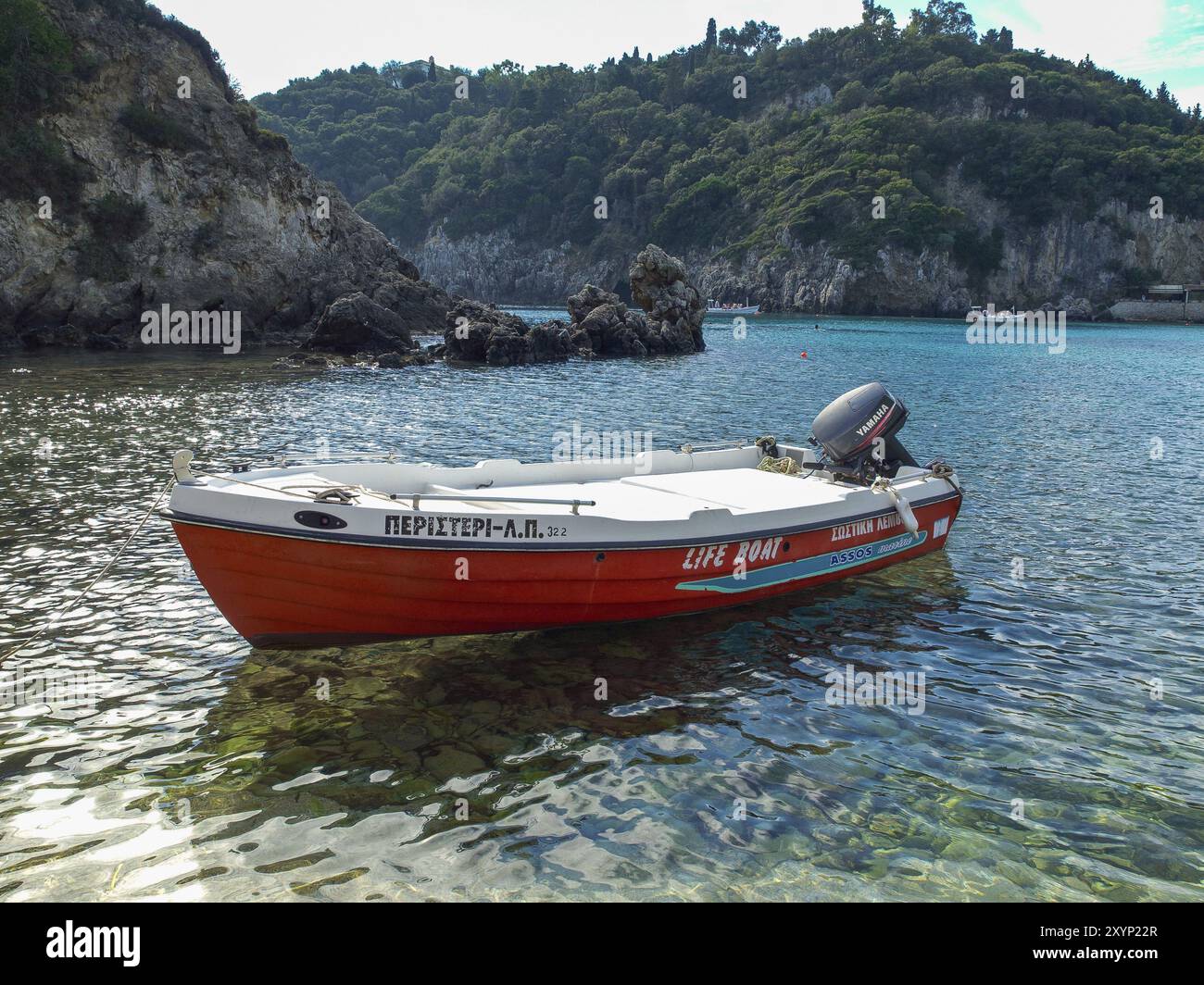 A red boat floats safely in the clear blue water with rocky structures ...