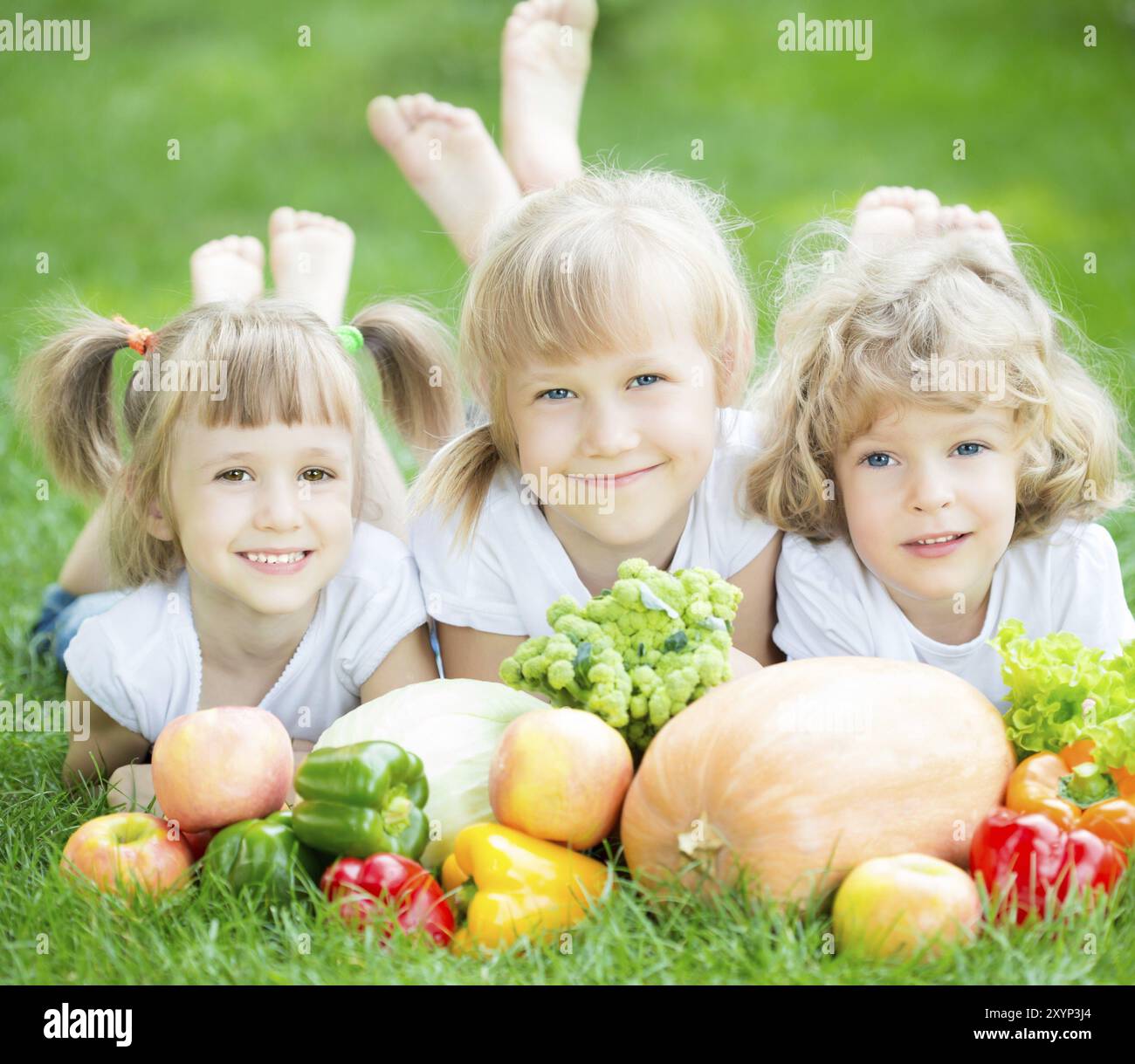 Group of happy children with fruits and vegetables lying on green grass ...